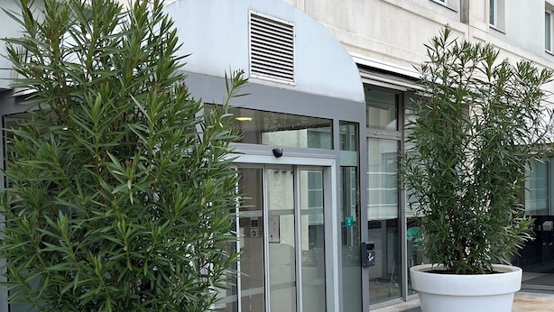 Entrada de um edifício com porta giratória, grandes vasos de plantas e um design arquitetônico moderno.