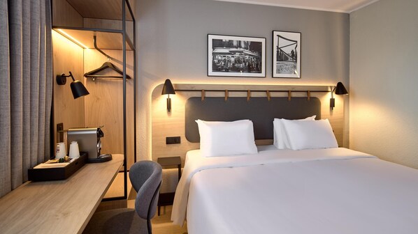 Quarto de hotel com cama, escrivaninha e cadeira. Duas imagens emolduradas na parede.