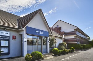 Um hotel chamado 'Kyriad' com uma área de recepção, uma placa indicando um restaurante e um estacionamento.