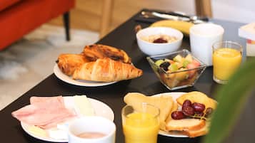Uma mesa de café da manhã com croissants, presunto, queijo, uma tigela de frutas e um copo de suco de laranja.