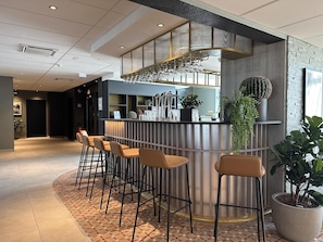 Uma área de bar moderna com banquetas, um balcão com copos e plantas decorativas.