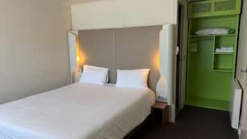 Quarto de hotel com cama, mesas de cabeceira, um armário verde e um radiador branco.