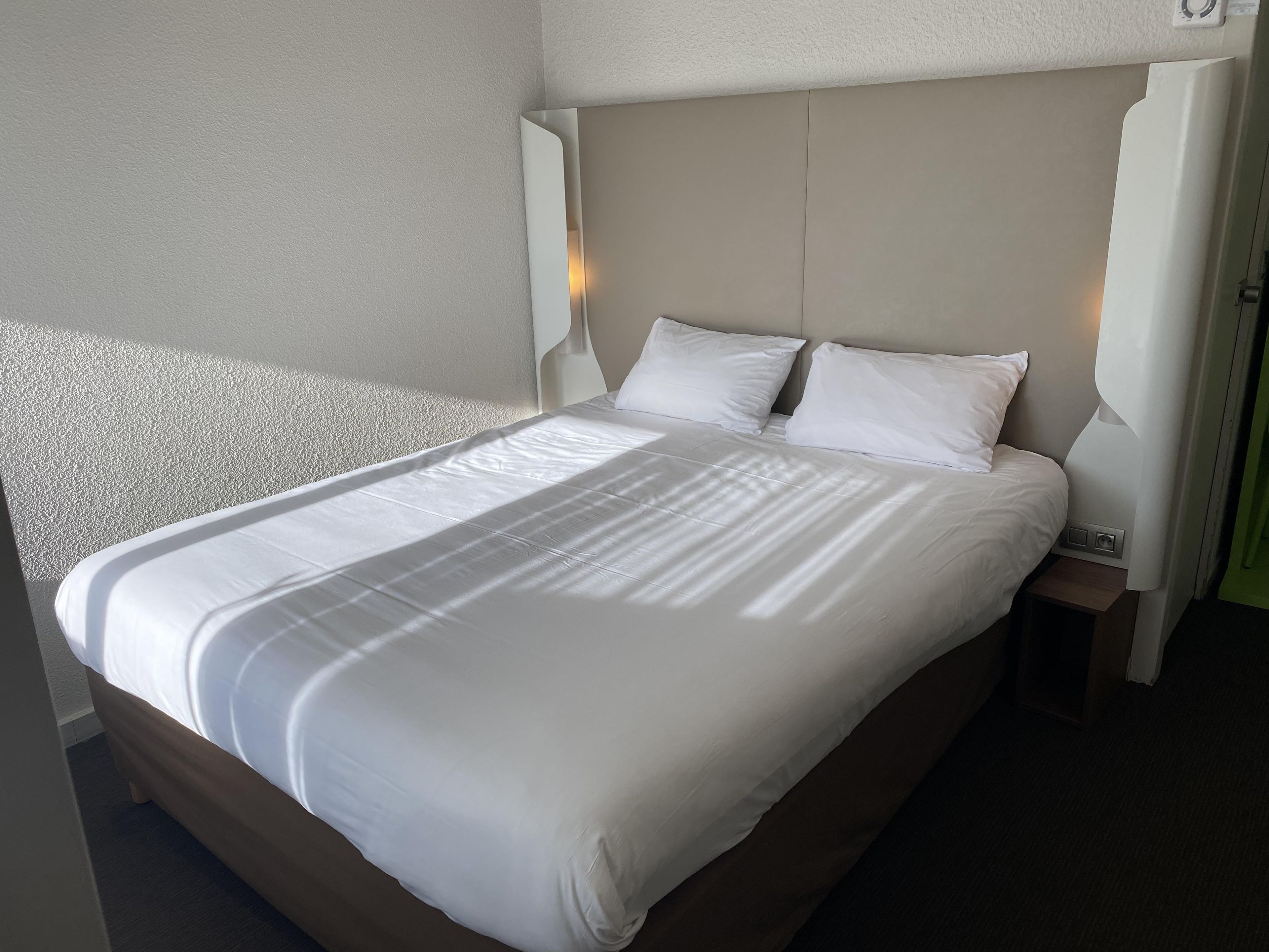Cama bem arrumada com lençóis brancos, cabeceira e abajures.