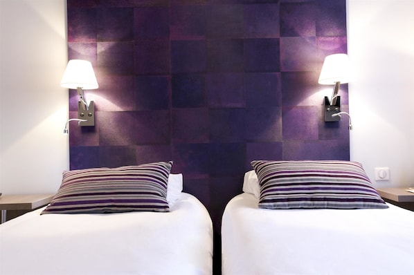 Quarto de hotel com duas camas, cada uma com almofada listrada, e uma parede texturizada grande ao fundo.