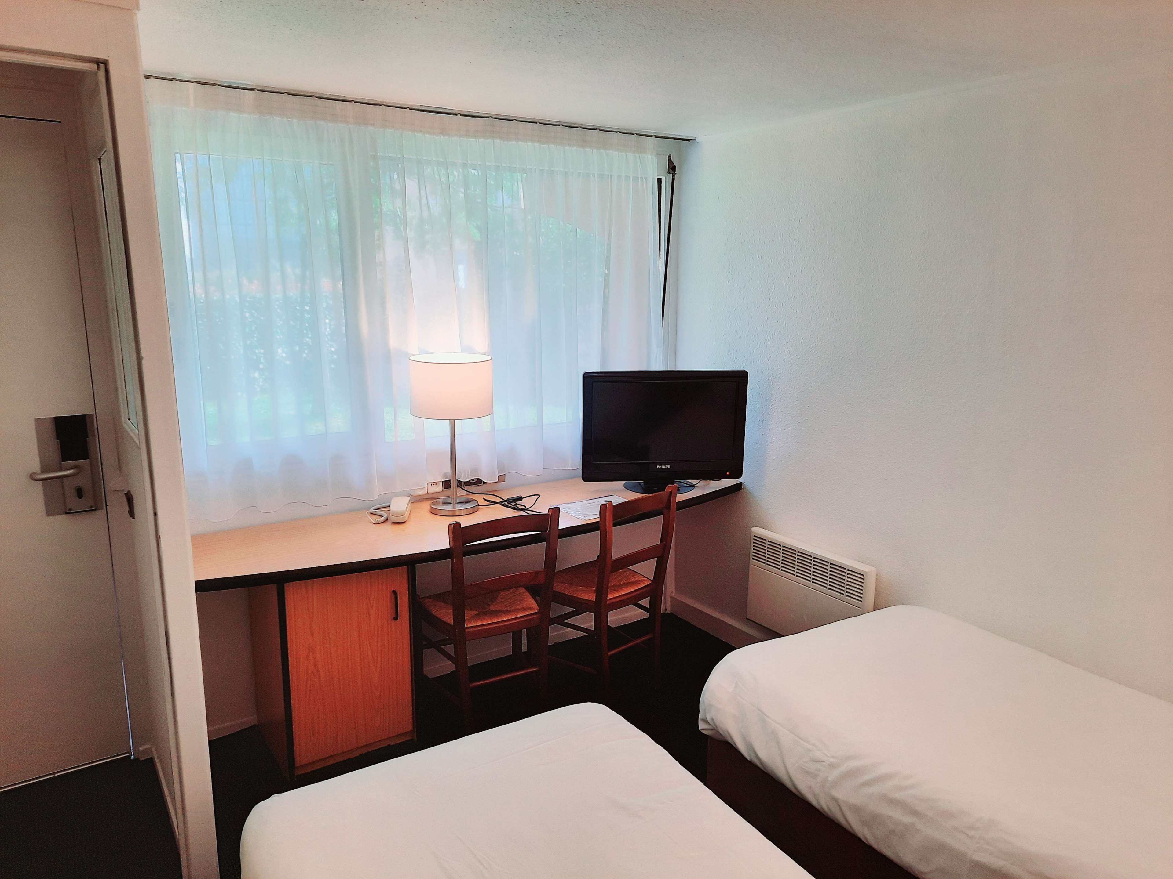 Quarto de hotel com escrivaninha, uma cadeira, televisão e duas camas.