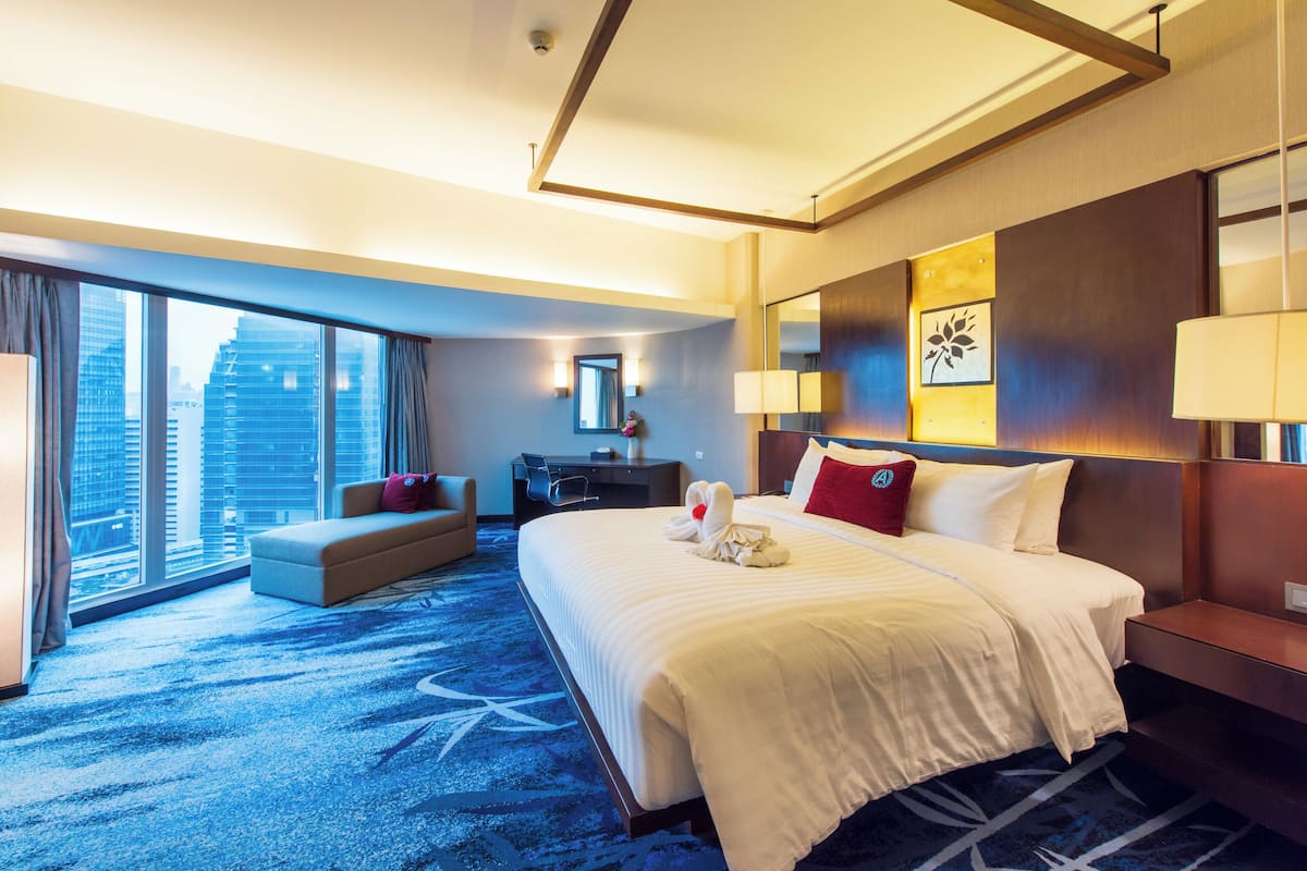 Quarto de hotel com uma cama grande, área de estar, escrivaninha e vista para a paisagem urbana.