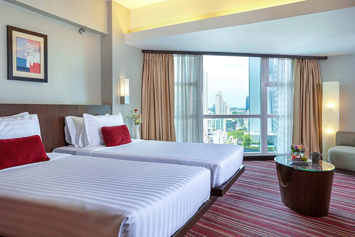 Quarto de hotel com duas camas, vista da cidade e uma mesa de centro moderna.