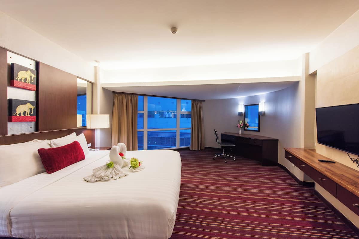 Quarto de hotel com uma cama grande, uma escrivaninha, televisão e vista para a paisagem urbana pela janela.