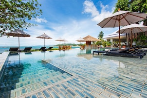 Uma área à beira da piscina com espreguiçadeiras, guarda-sóis e vista para o mar.