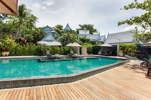 Piscina com espreguiçadeiras e guarda-sóis, cercada por plantas tropicais e arquitetura tradicional.