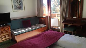Quarto de hotel com cama, sofá, escrivaninha, televisão e janela com cortinas.