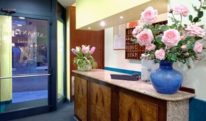 Balcão de recepção com um vaso azul de flores rosa, bancada de madeira e porta de vidro com um logotipo.