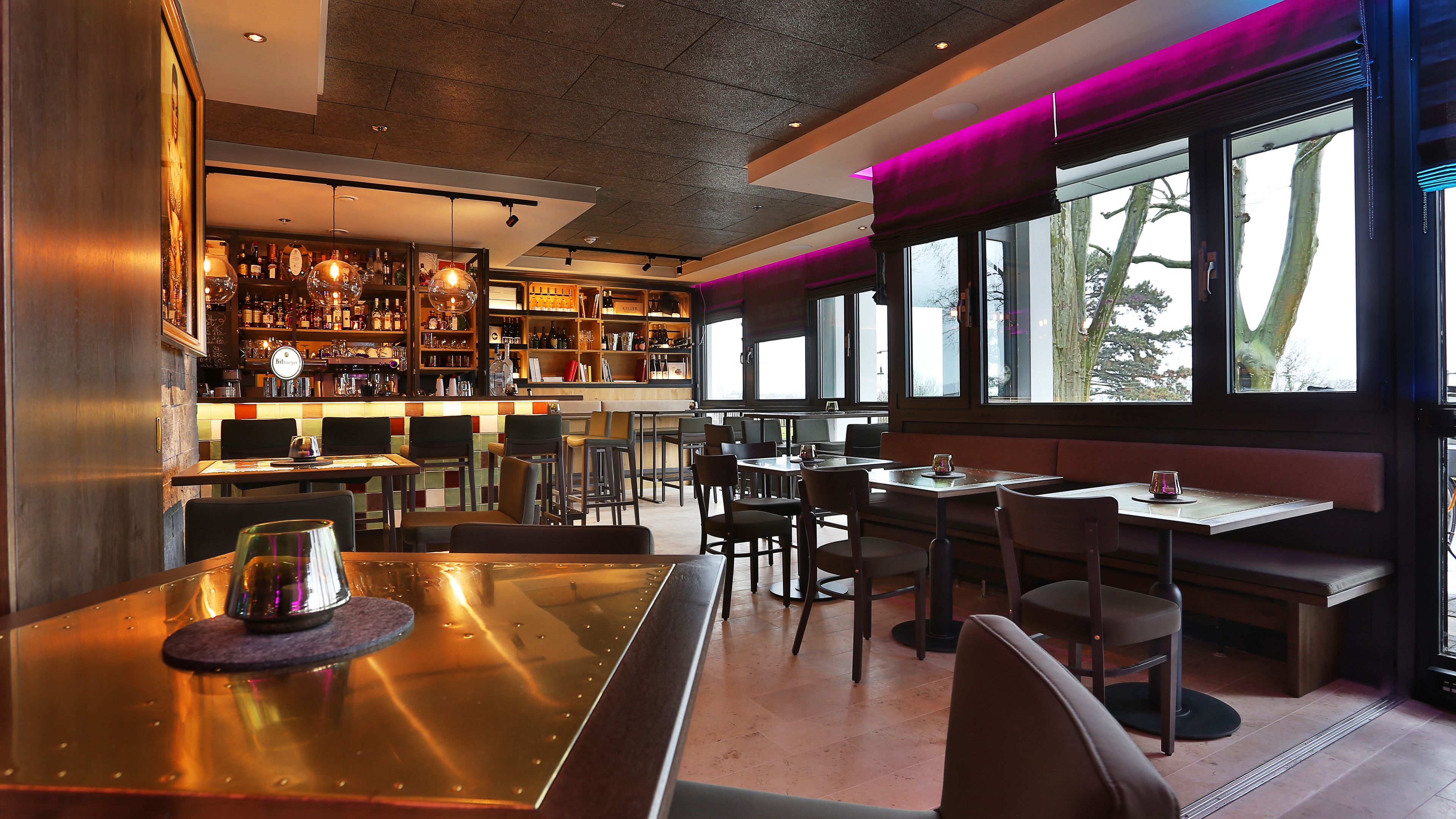 Restaurante com área de bar, assentos e grandes janelas.