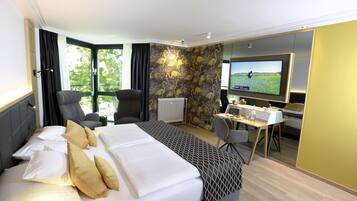 Quarto de hotel com uma cama grande, uma escrivaninha com computador, televisão e vista para o verde lá fora.