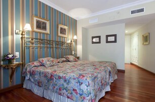 Quarto com colcha florida, papel de parede listrado e piso de madeira.