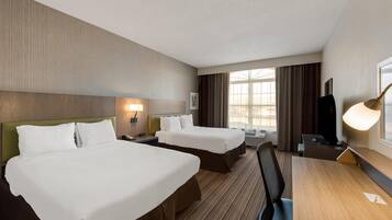 Quarto de hotel com duas camas, uma escrivaninha, uma cadeira, uma televisão e uma janela com cortinas.
