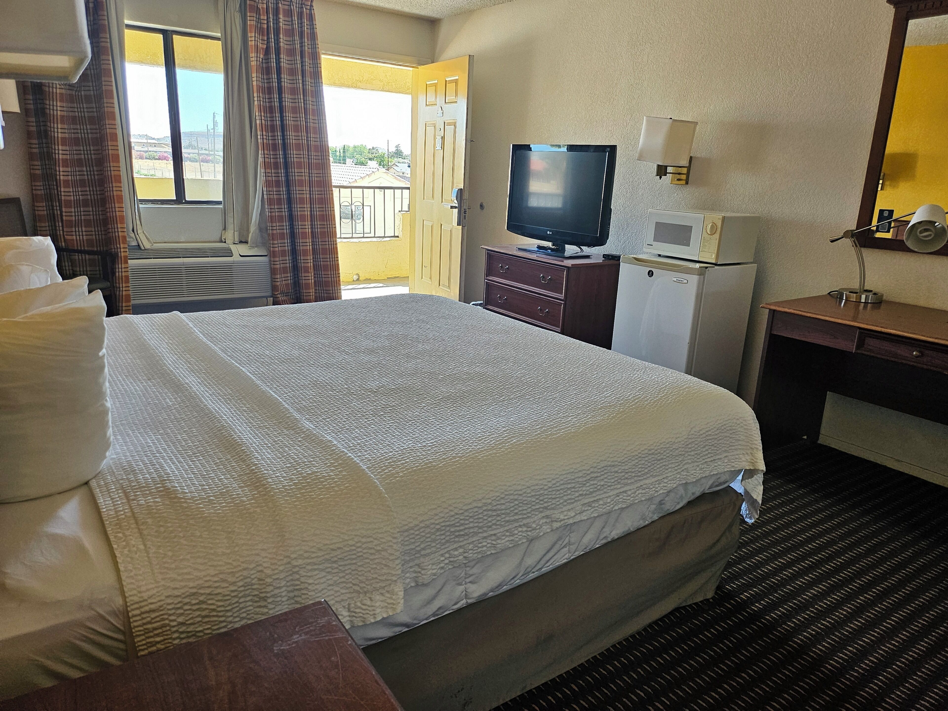 Quarto de hotel com cama, escrivaninha, televisão, micro-ondas e vista para o exterior.