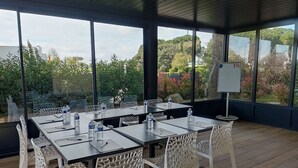 Sala de conferência com grandes janelas, cadeiras brancas e mesas dispostas para reuniões.