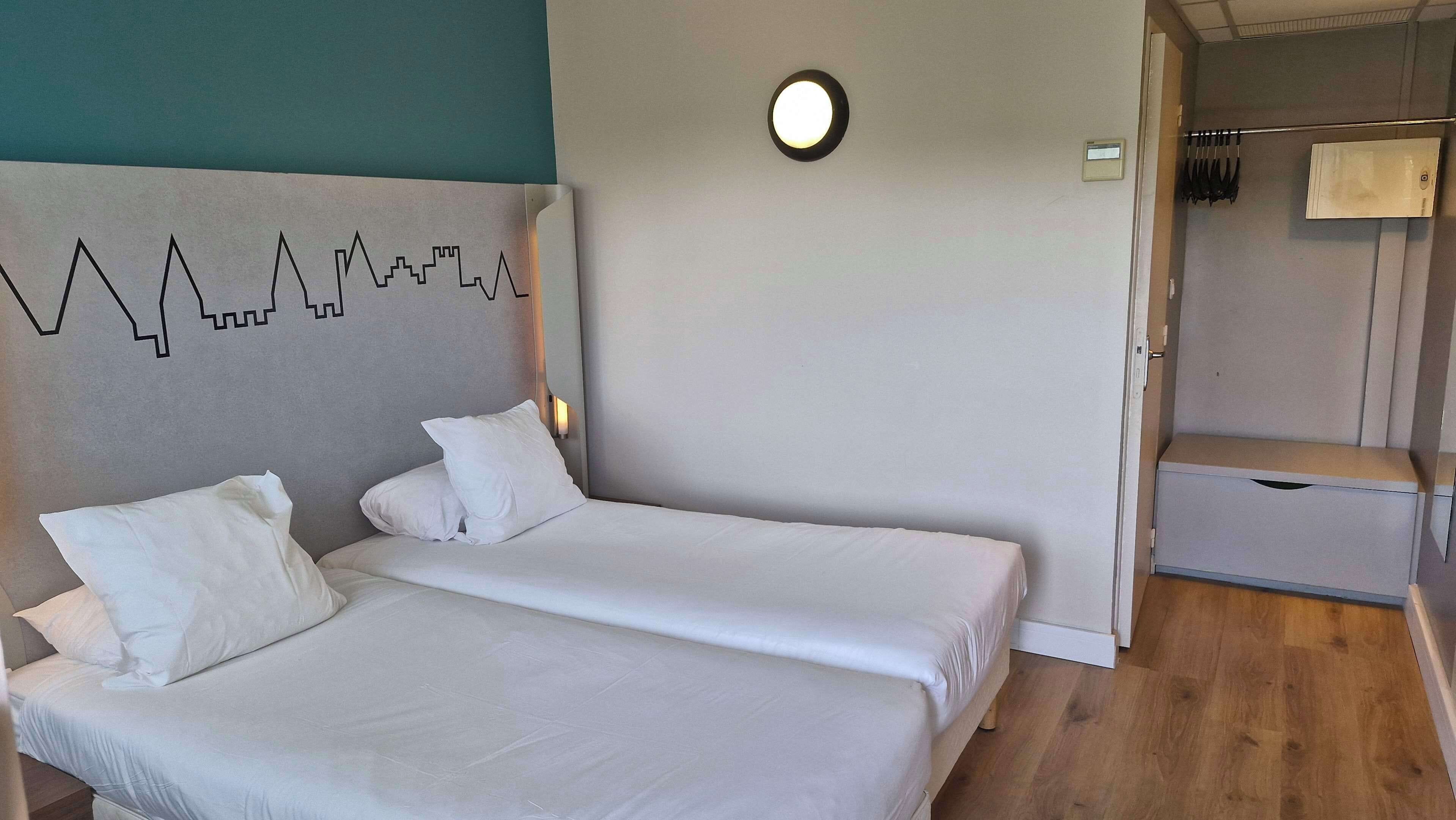 Quarto de hotel com cama, cabeceira com design da paisagem urbana, mesa de cabeceira e pequena escrivaninha com cadeira.