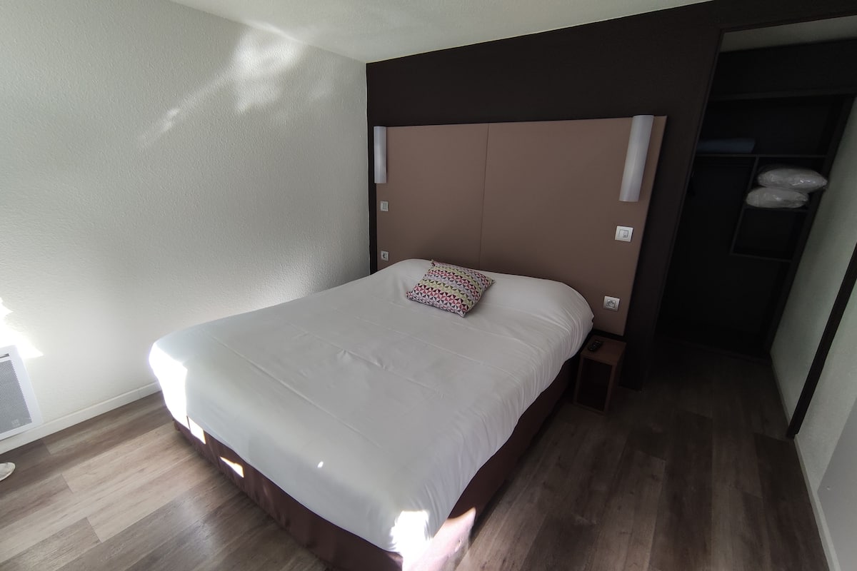 Cama bem arrumada com travesseiro estampado em quarto com piso de madeira e cabeceira marrom.