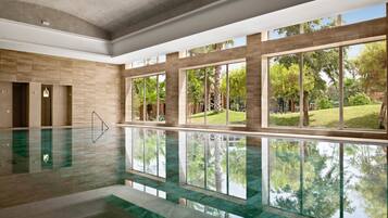 Piscina interna ampla com grandes janelas que oferecem vista para um jardim paisagístico.