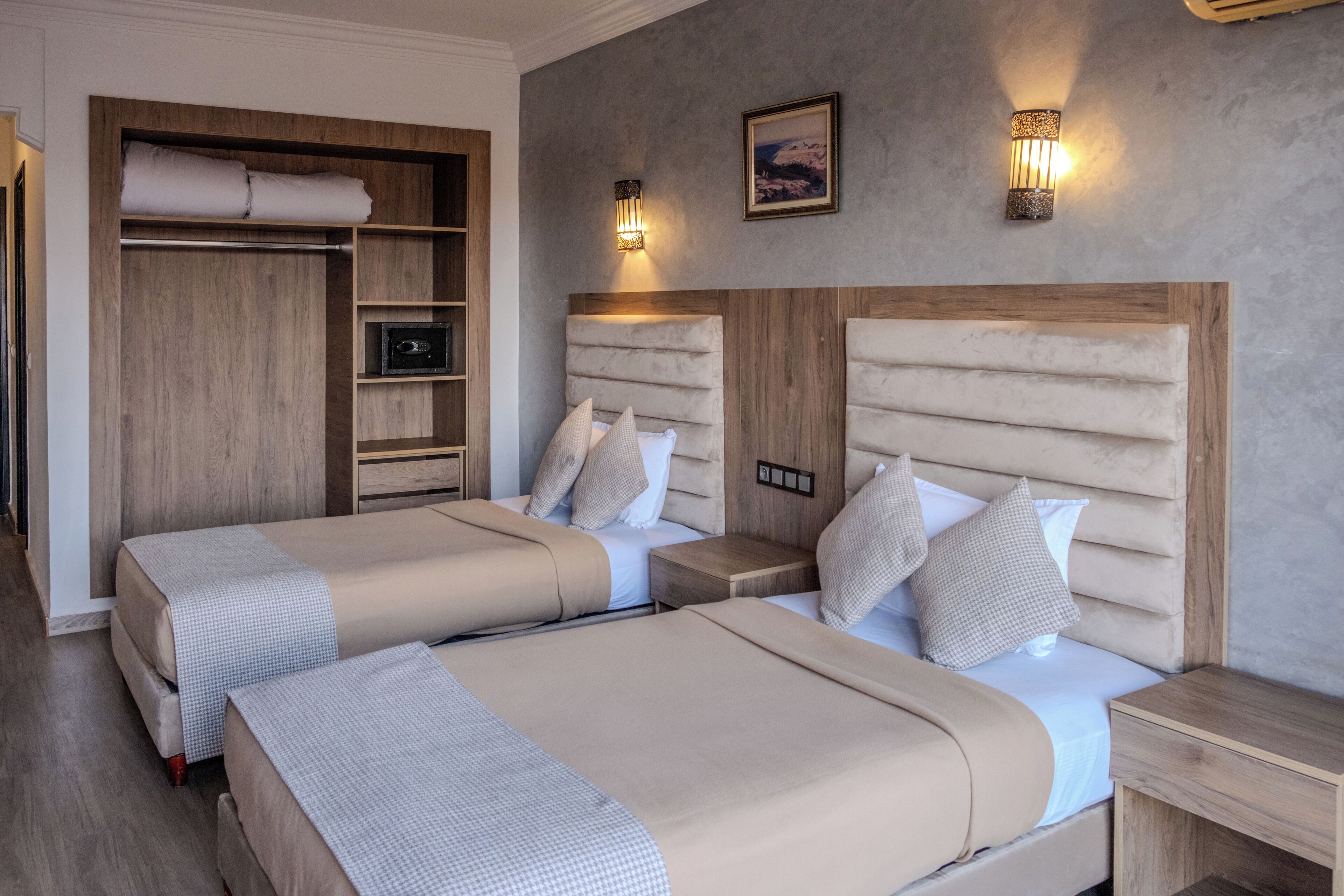 Quarto de hotel com duas camas, um guarda-roupa de madeira, uma estante embutida e iluminação na parede.