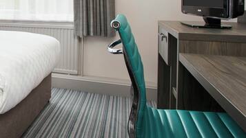Quarto de hotel com cama, escrivaninha e cadeira com apoio de cabeça.