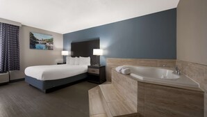 Quarto de hotel moderno com uma cama grande, banheiro separado com banheira e um quadro na parede.