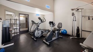 Uma academia com equipamentos de exercícios, um bebedouro e um suporte fixado na parede.