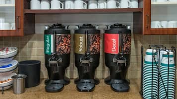 Três dispensadores de café identificados como Tradicional, Intenso e Descafeinado em uma cozinha, com uma cafeteira e xícaras sobre o balcão.