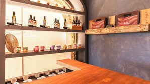 Uma área de bar com prateleiras exibindo garrafas e potes, um balcão de madeira e uma parede rústica com painéis de madeira.