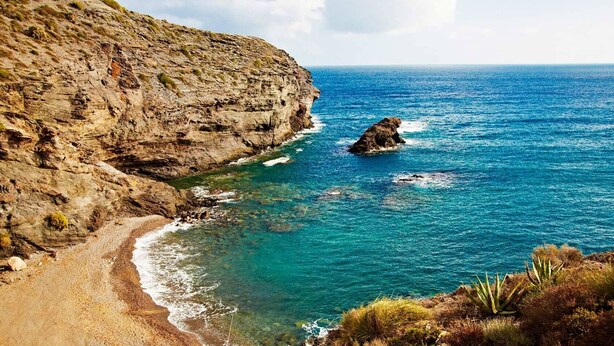 Paisagem costeira com um penhasco rochoso e mar azul cristalino.