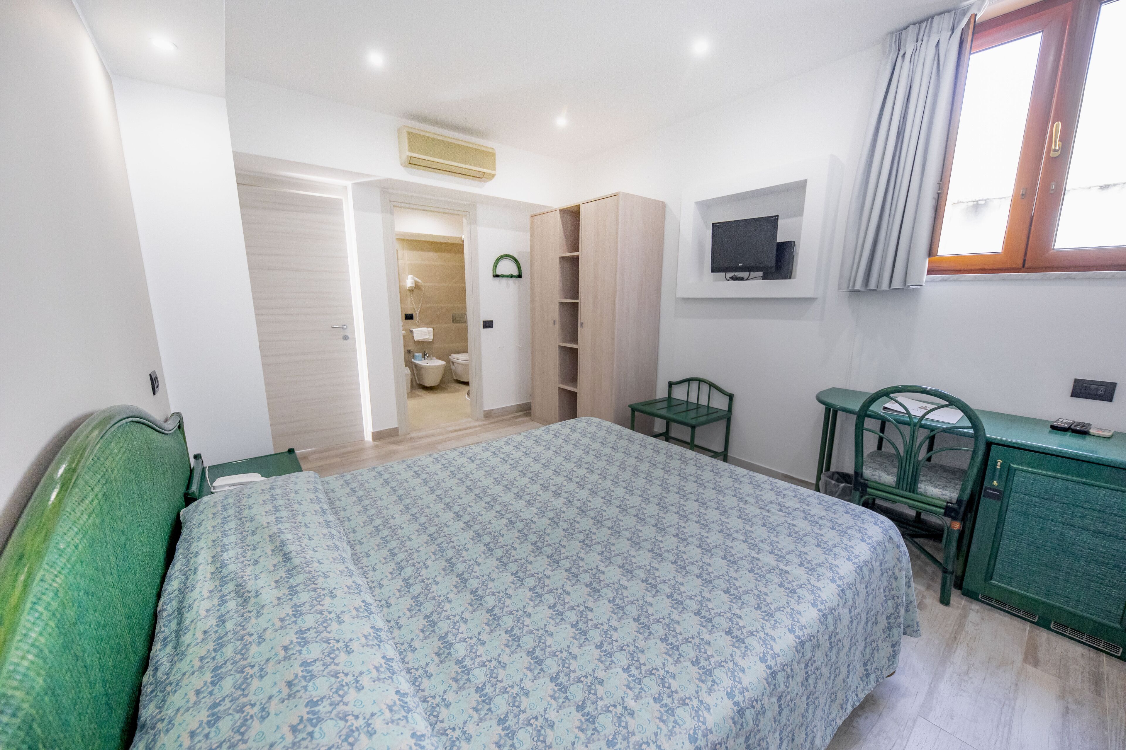 Quarto com cama, escrivaninha, cadeira, televisão e guarda-roupa.