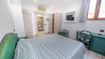 Quarto com cama, escrivaninha, cadeira, televisão e guarda-roupa.
