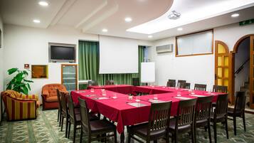 Uma sala de conferências com uma mesa comprida, cadeiras, uma televisão e uma tela de projeção.