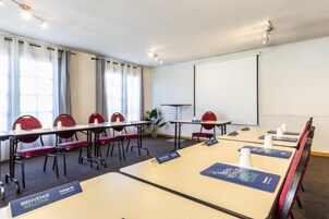 Uma sala de conferências com mesas, cadeiras, etiquetas de nome e uma tela de projetor.