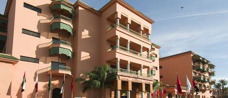 Hotel de vários andares com varandas, bandeiras e um céu claro.