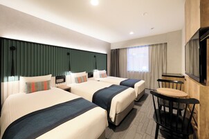 Quarto de hotel com três camas, uma escrivaninha e uma televisão.