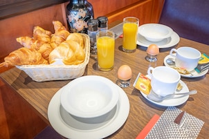 Uma mesa de café da manhã com croissants, suco de laranja, ovos e xícaras de café.