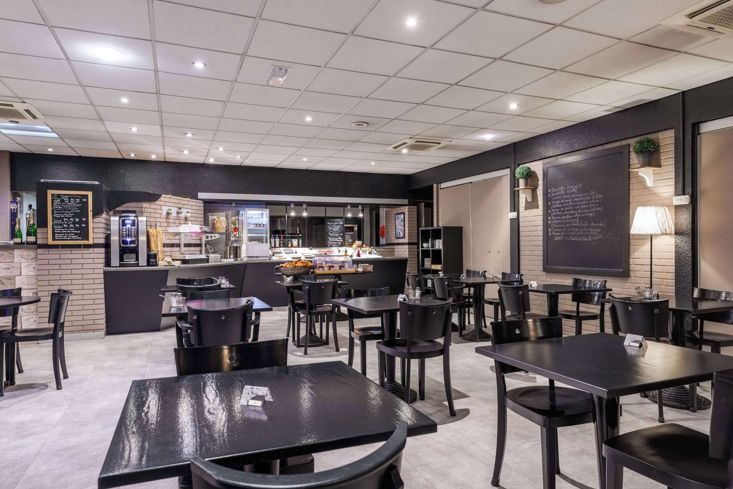 Interior de restaurante moderno com balcão central, mesas e cadeiras pretas e um menu em lousa.