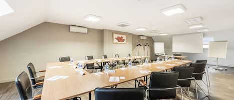 Uma sala de conferências com uma mesa comprida, cadeiras pretas e uma tela de projetor.