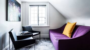 Uma sala de estar moderna com um sofá roxo, uma cadeira preta e uma pequena mesa redonda.