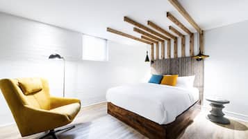 Quarto moderno com cabeceira de madeira, poltrona amarela, cama grande com roupa de cama branca e luminária de chão.