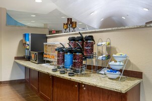 Uma mesa de pequeno-almoço com dispensadores de café, micro-ondas e uma variedade de fruta.