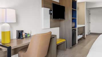 Quarto de hotel com escrivaninha, cadeira, televisão e uma pequena cozinha equipada.