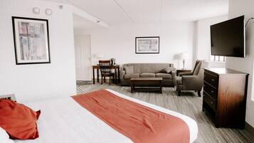 Quarto de hotel com cama, sofá, poltrona, televisão e cômoda.