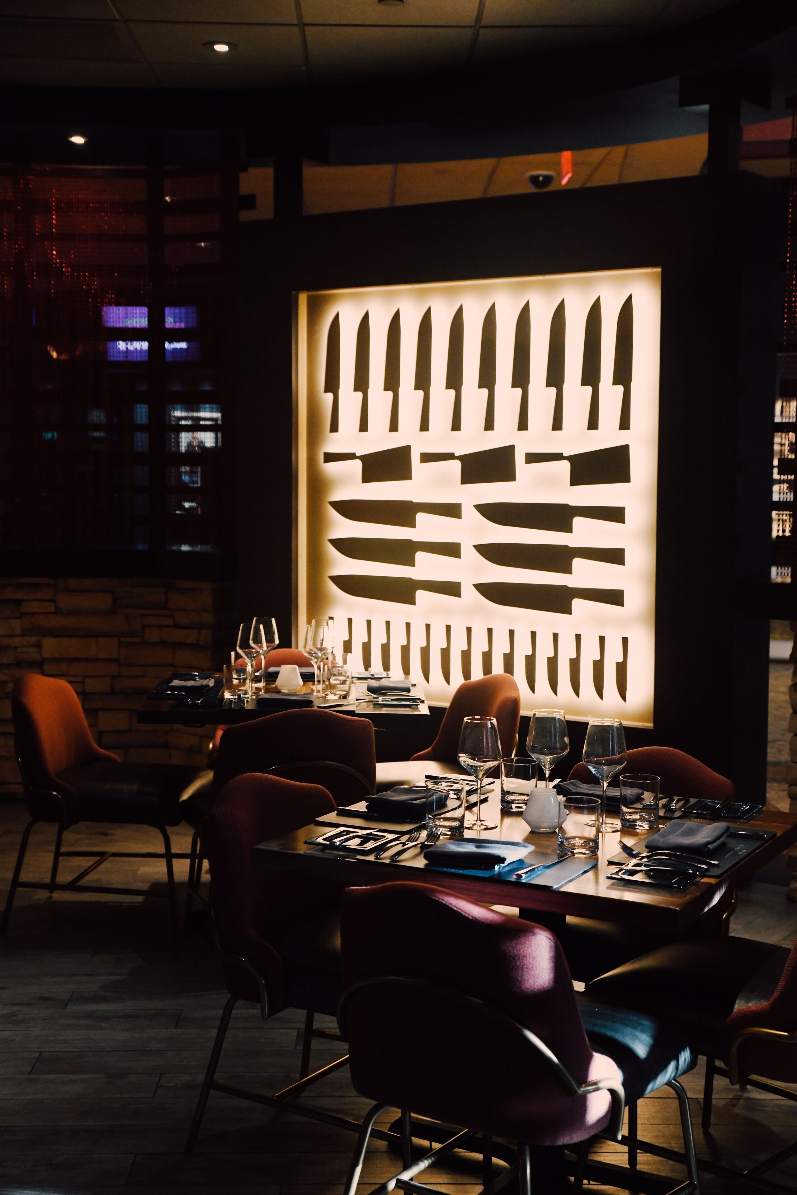 Restaurante com iluminação suave e interior moderno, apresentando uma mesa posta para refeição e uma parede decorativa com padrões recortados.