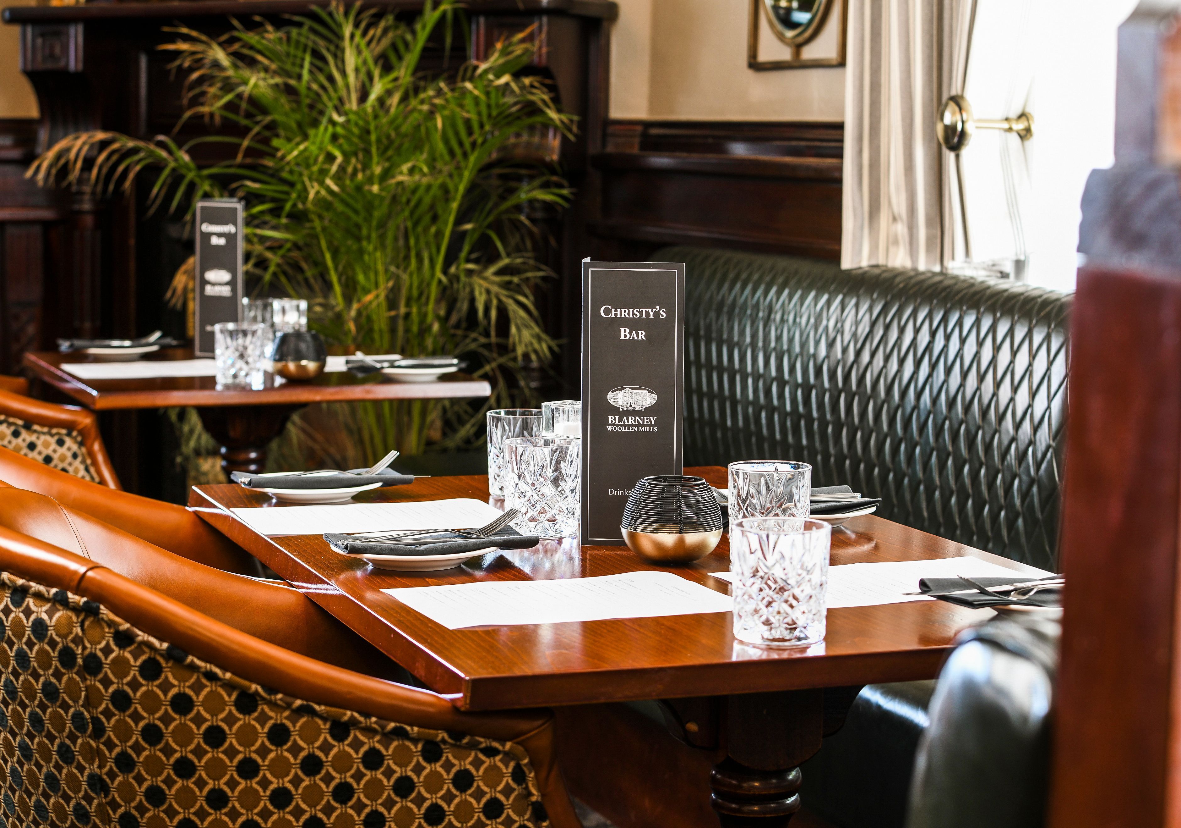 Um restaurante com mesa de madeira posta para refeição, um suporte para cardápio e um banco estofado verde.