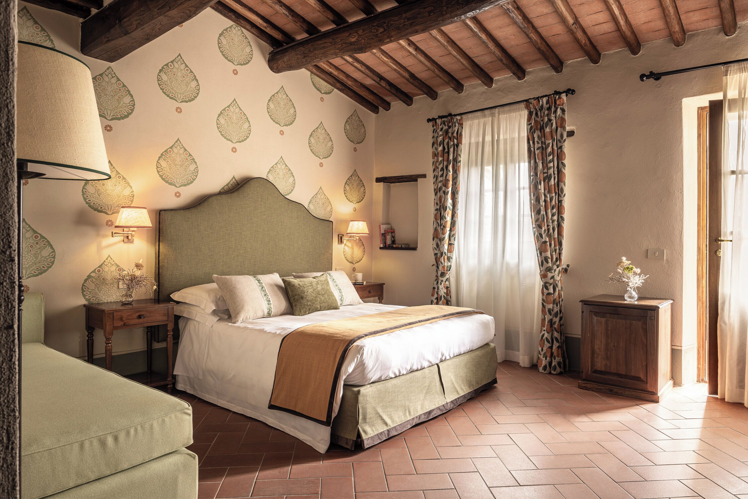 Quarto com cama, luminárias de cabeceira, mesa de cabeceira, cadeira, armário de madeira e papel de parede estampado.