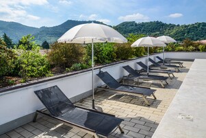 Terraço no telhado com espreguiçadeiras e guarda-sóis, com vista para uma paisagem montanhosa.